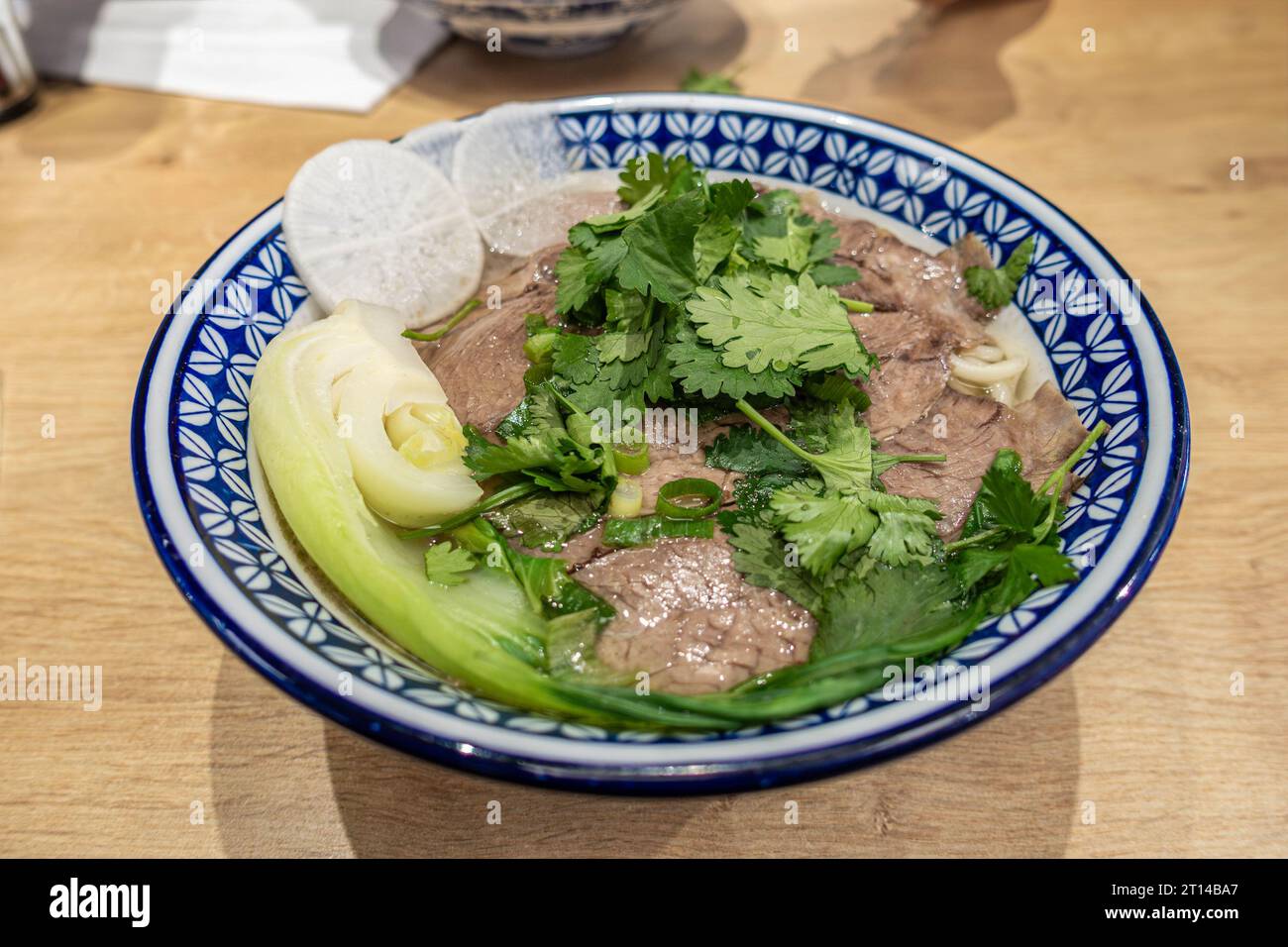 A bowl of Asian noodles with sliced beef, pak choi, sliced radish in a ...