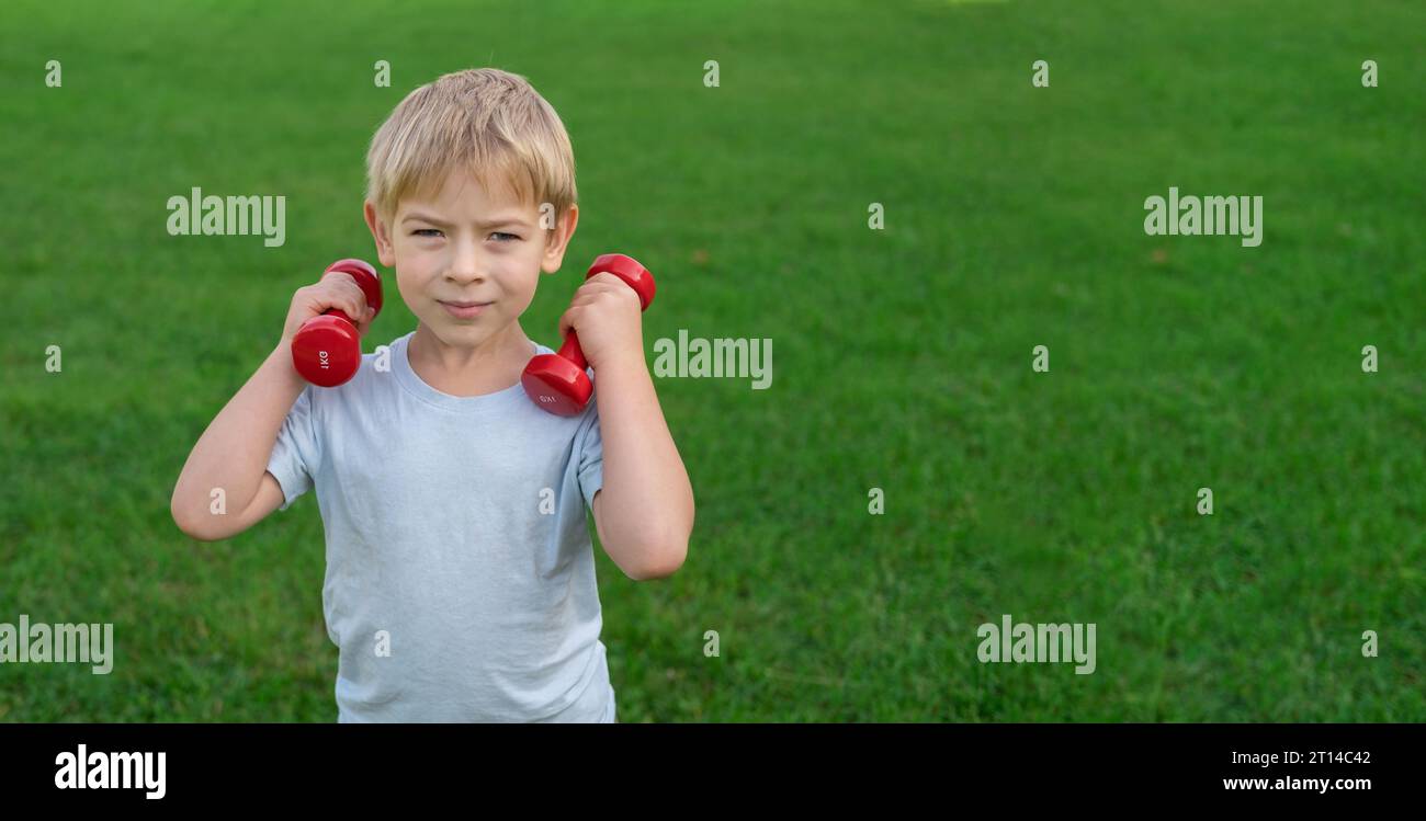 Sporty little boy lifting dumbbells on a green lawn. Joyful toddler ...