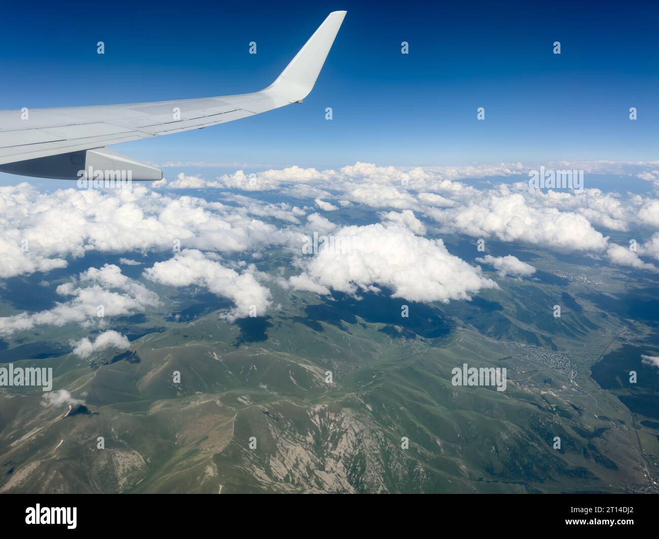 White wing from airplane window with mountain range below on sunny day ...