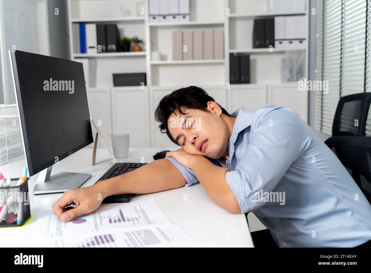 Young adult Asian businessman sleeping on his desk with a computer pc ...