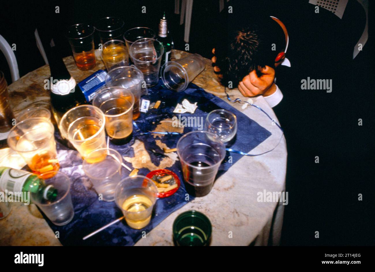 1990s UK a drunk student holds his head and rests it on a table covered ...
