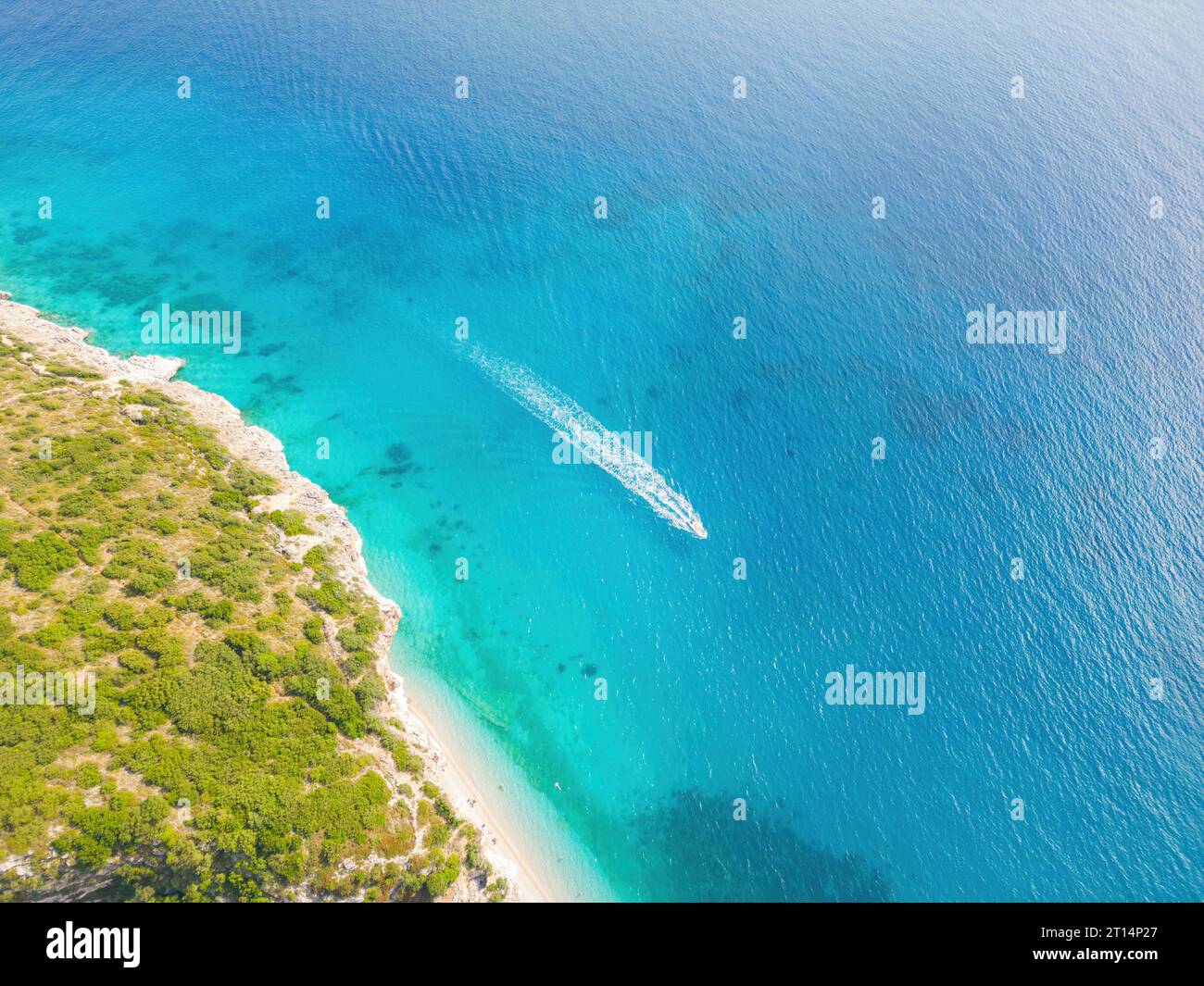 Aerial view of a clear blue sea. A boat leaving a white trail and a ...