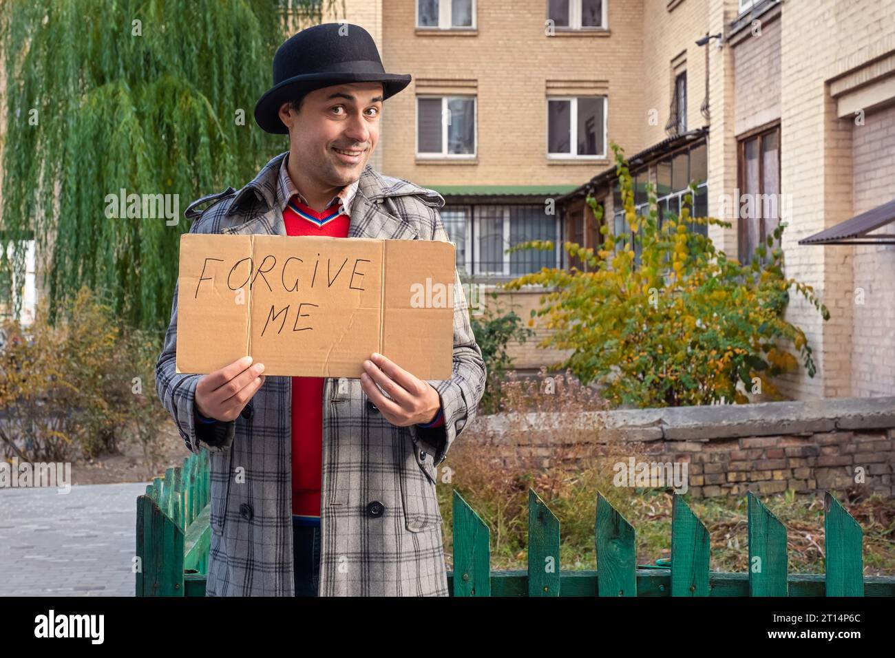 Cheerful man holding a sign with the text forgive me on the city street ...