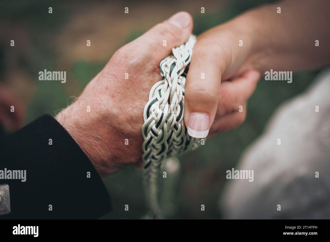 Close up picture of bride and groom's hands tied with white and green ...