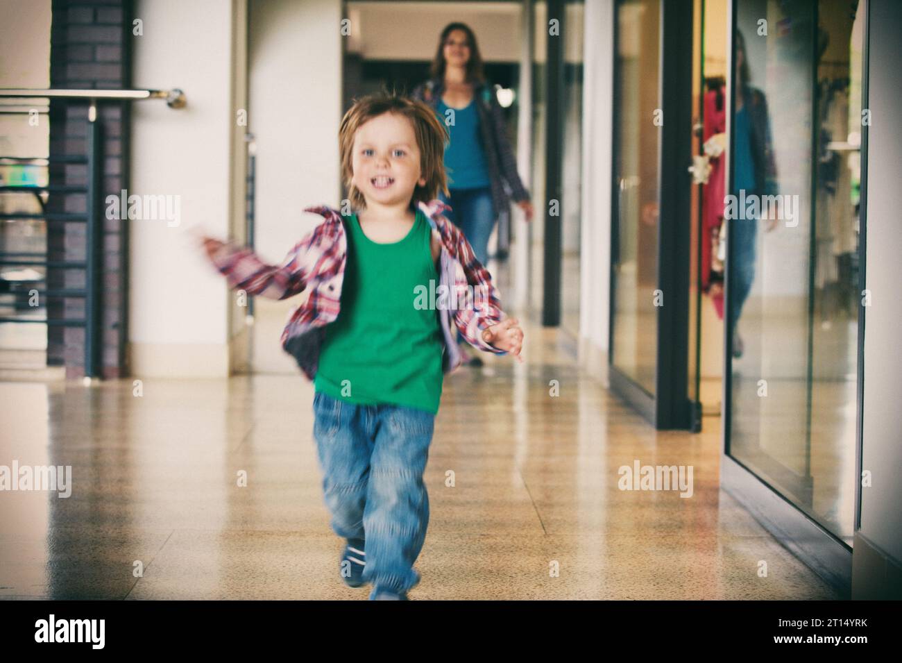 Little boy running in the shopping center with his mom on background ...