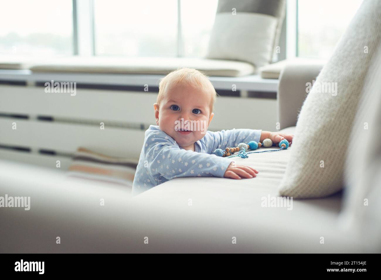 Little 8 months baby boy stands with support near sofa at home in white ...