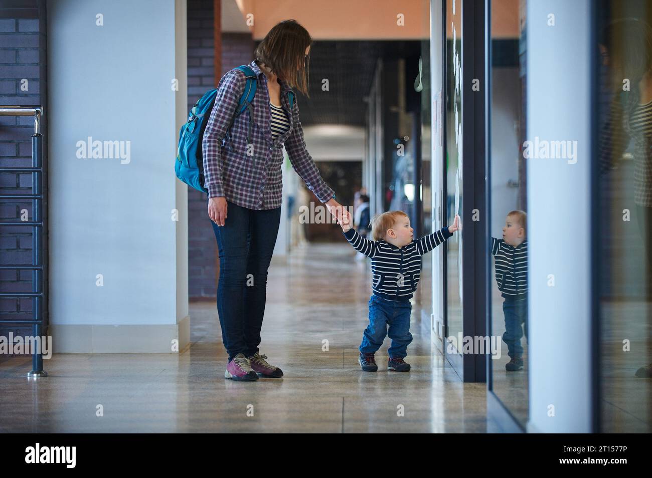 Toddler walking in the shopping center with his mom. Mother takes the ...