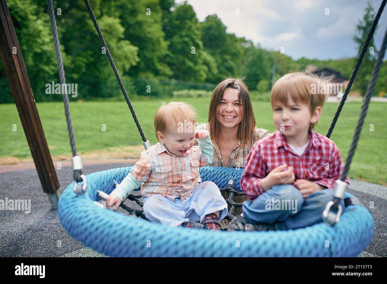 Mom and children playing with sons on a swing at the playground Stock Photo - Alamy