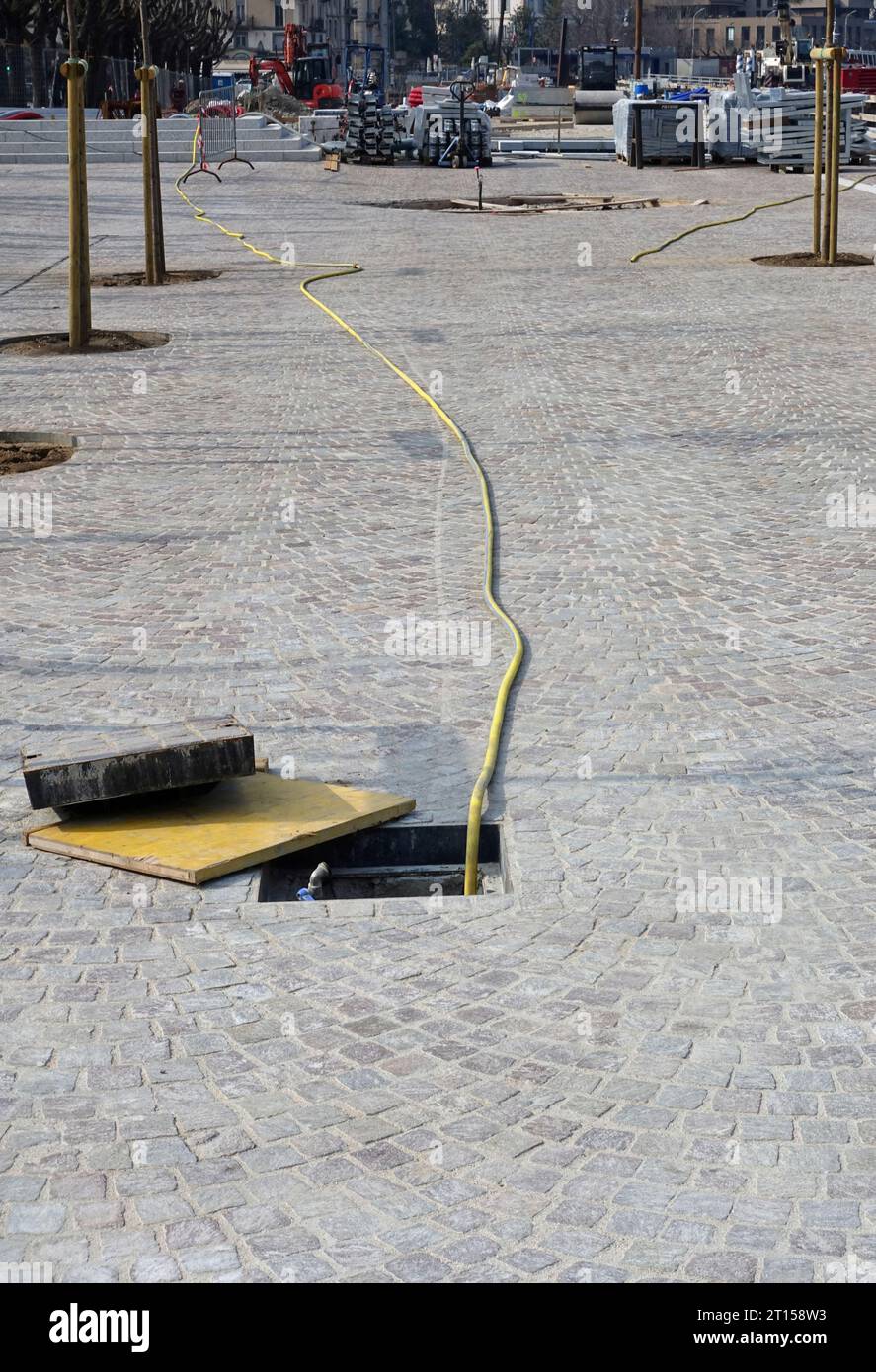 long hose inside an open manhole in cobblestone street Stock Photo - Alamy