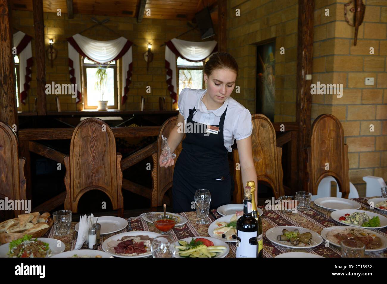 Young waitress in uniform setting the table. Restaurant banquet hall in ...