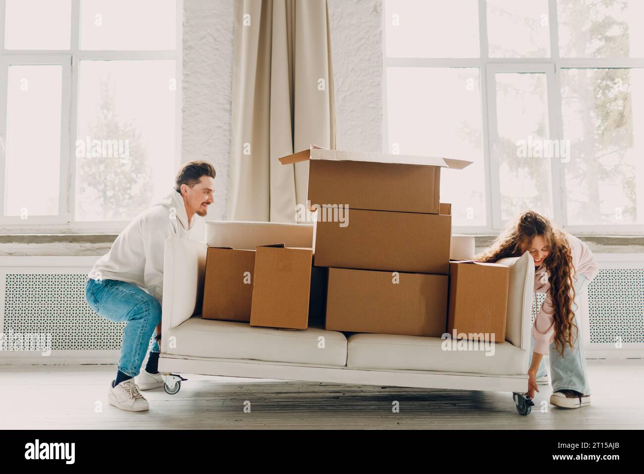 Happy young family couple man and woman push sofa with cardboard boxes ...