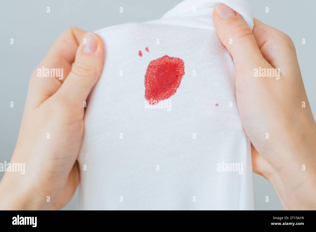 Drop stain of blood on a white cloth. Female hands hold soiled clothes ...