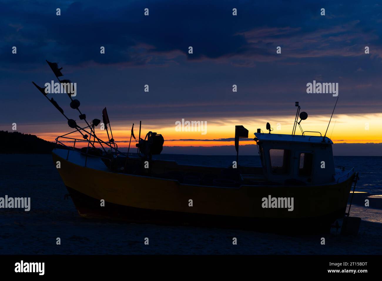A yellow-orange fishing boat pulled up on the beach during sunset ...