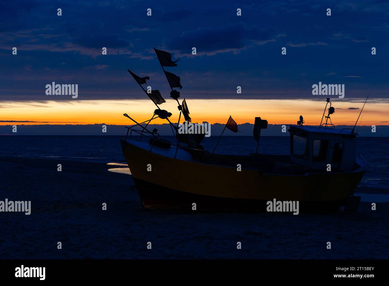 A yellow-orange fishing boat pulled up on the beach during sunset ...
