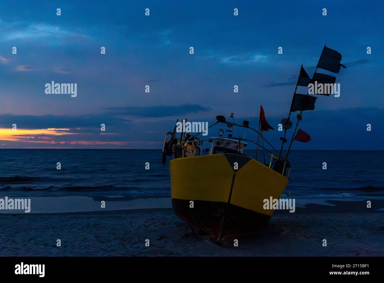 A yellow-orange fishing boat pulled up on the beach during sunset ...