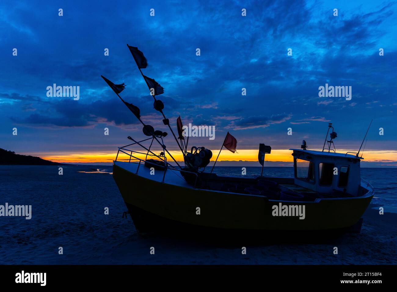 A yellow-orange fishing boat pulled up on the beach during sunset ...