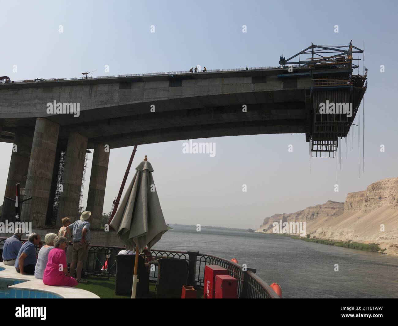 A cruise ship sails underneath the overhanging span of a road bridge under construction on the ...