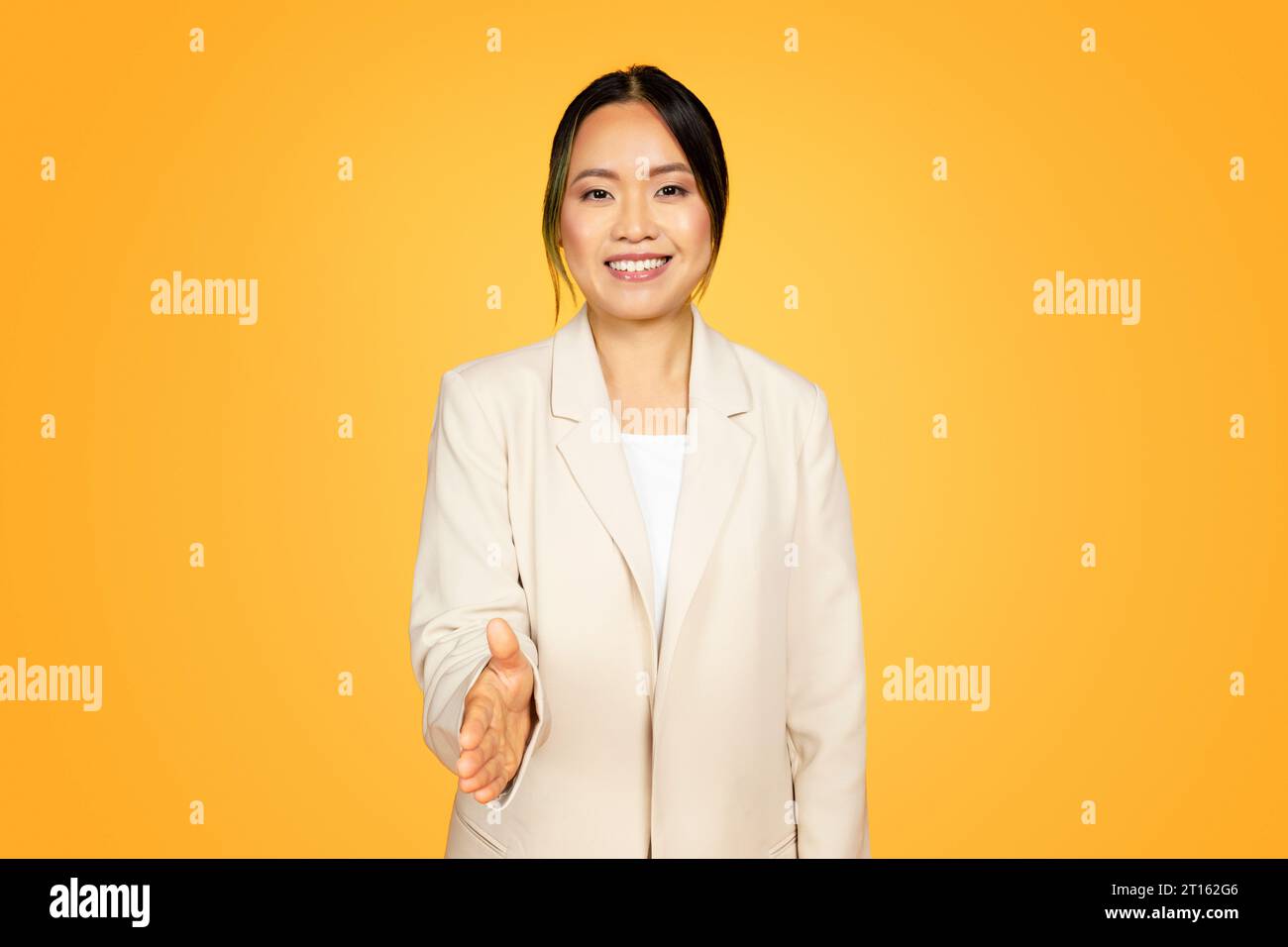 Millennial Asian woman in yellow, extending hand warmly for a handshake ...