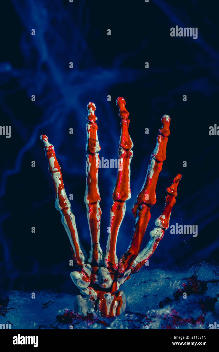 Bloodied skeleton hand in front of artificial cobwebs, blue background ...
