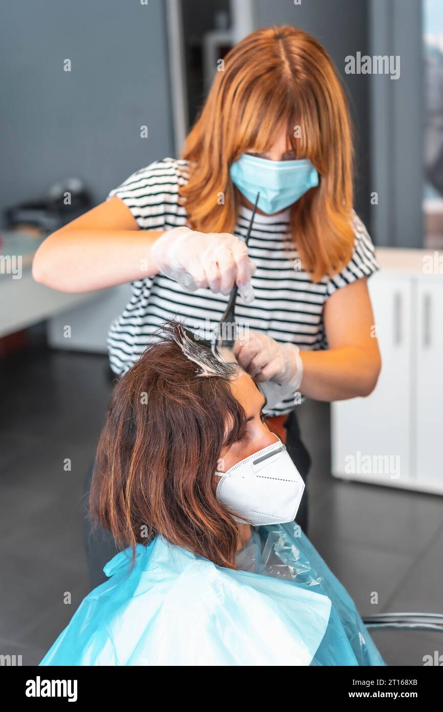 Caucasian hairdresser with face mask giving the dark tint to the client ...