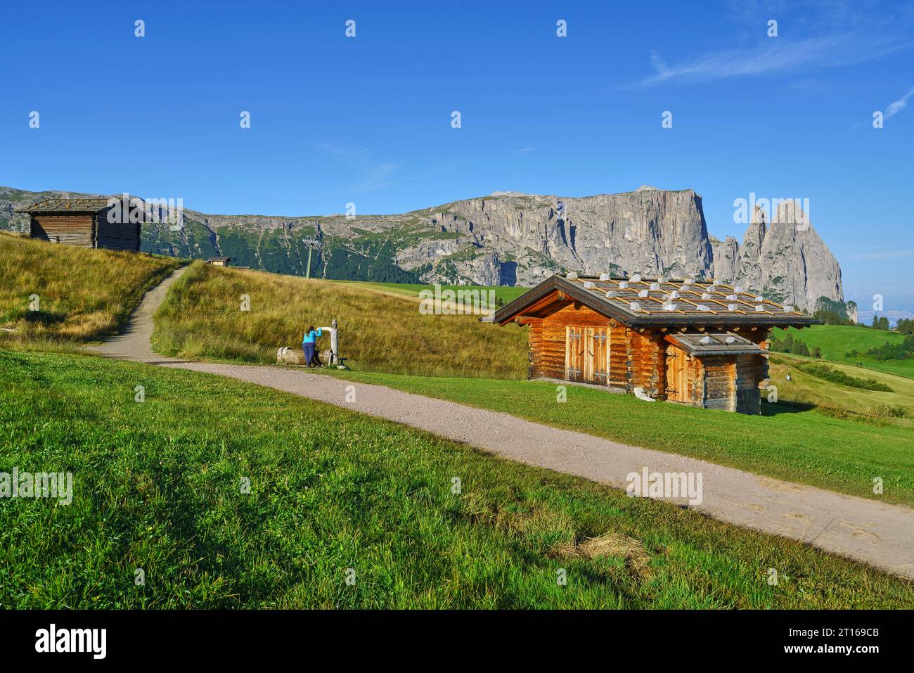Alpine hut in front of Schlern, woman drinking water from a well ...