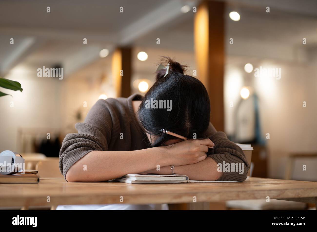 A tired and sleepy young Asian woman is falling asleep at a table while ...