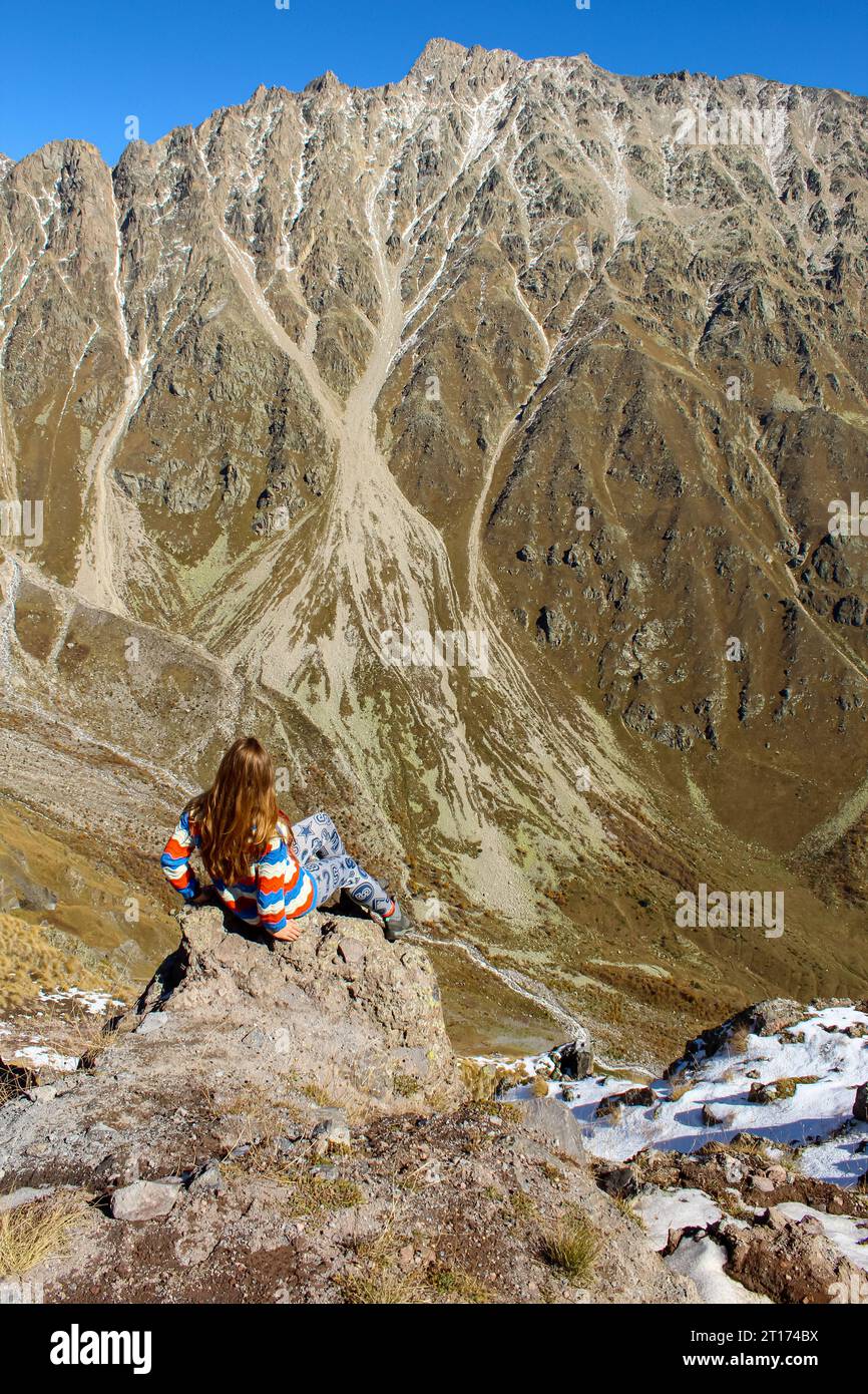 The girl sitting at the cliff of the huge rock overlooking the tall ...