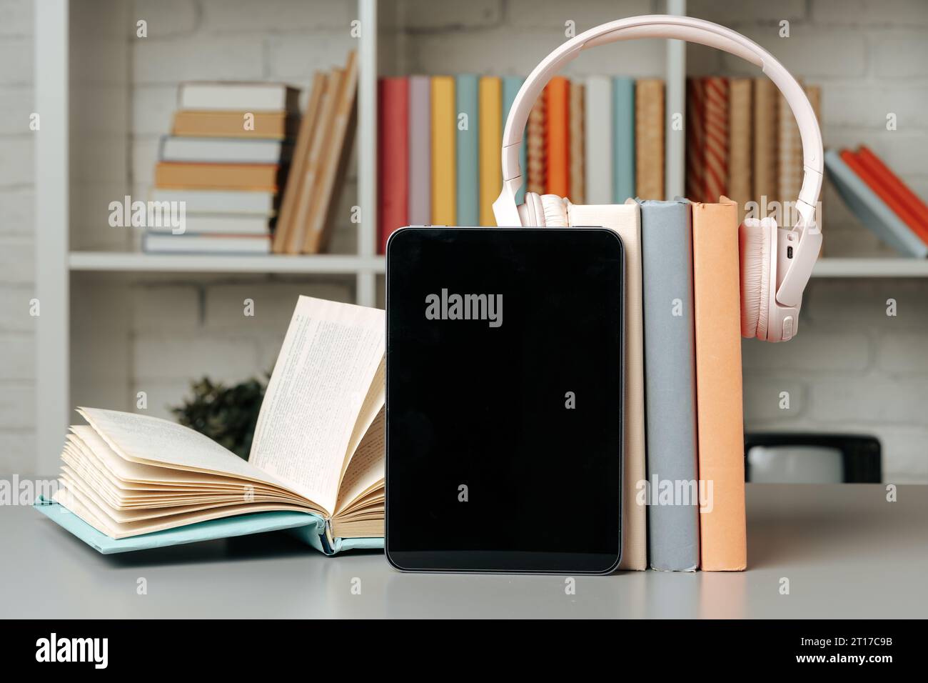 Digital tablet with stacked books in library Stock Photo - Alamy