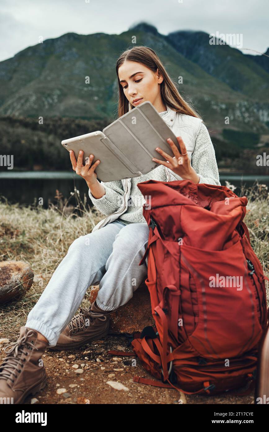Tablet, reading and woman hiking with backpack in nature on mountain ...