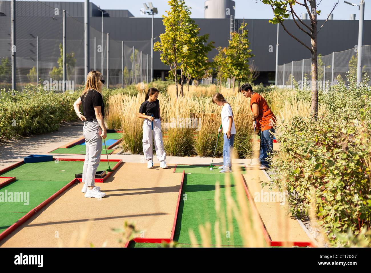 Group of smiling friends enjoying together playing mini golf in the ...