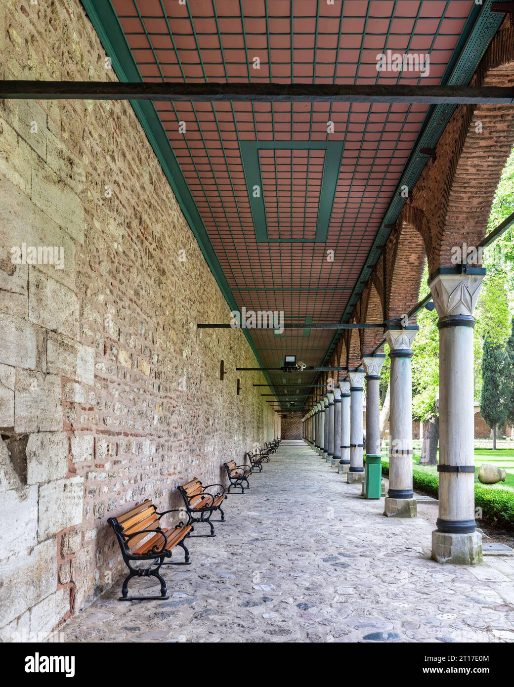 Long covered paved walkway with columns and benches. The walkway is ...