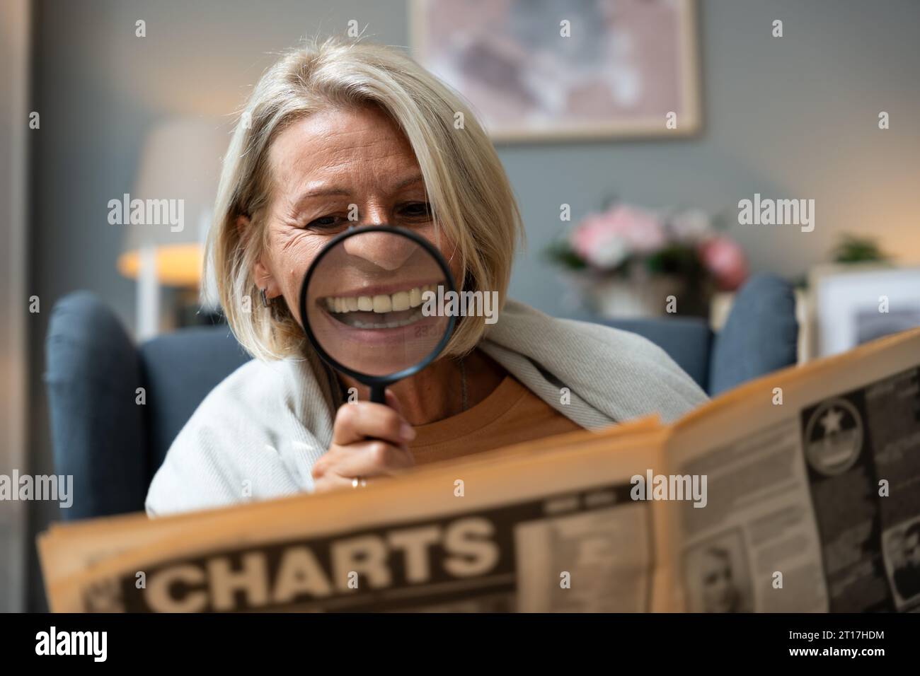 Senior woman reading newspaper with magnifying glass, unaware making ...