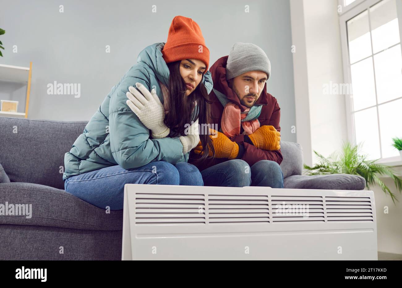 Freezing people warming themselves beside electric heater at home Stock ...