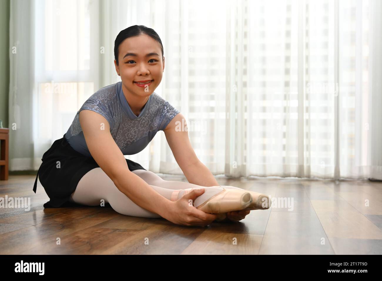 Beautiful ballerina sitting on the floor, warming up before dance class ...