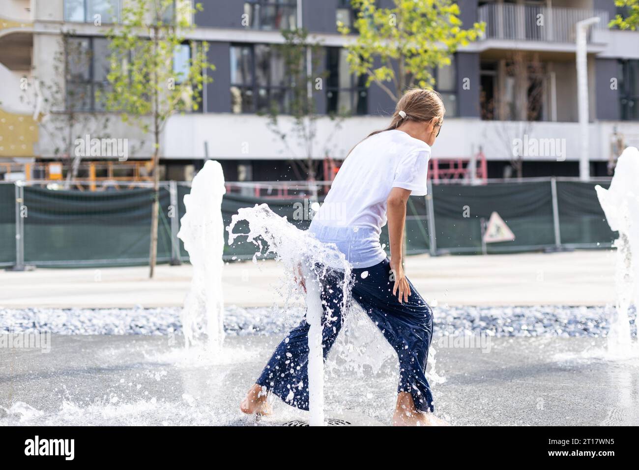 Cheerful young teen girl in city fountain, girl in wet clothes is ...