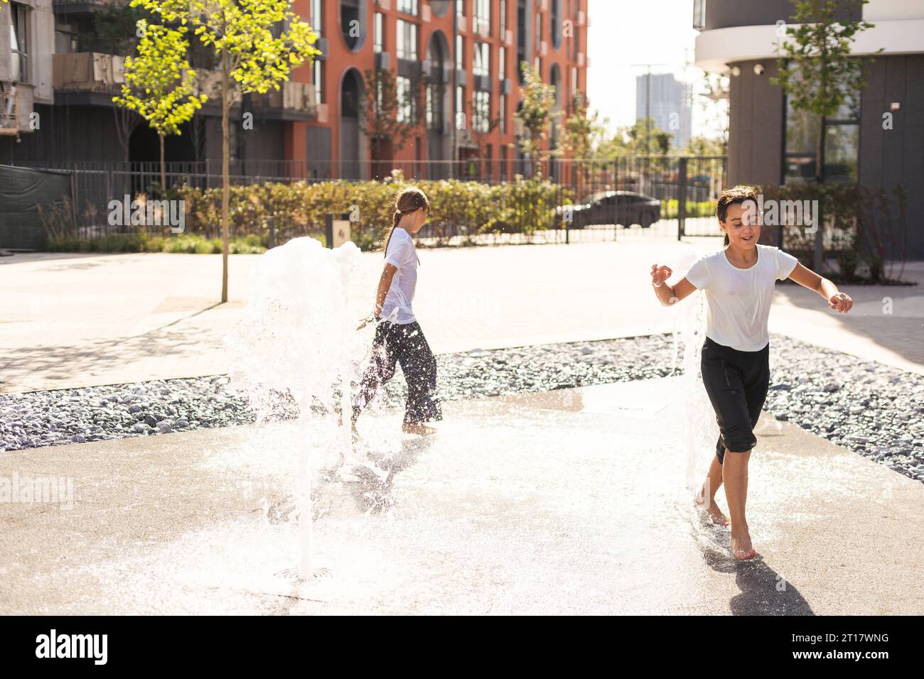 Cheerful young teen girl in city fountain, girl in wet clothes is ...