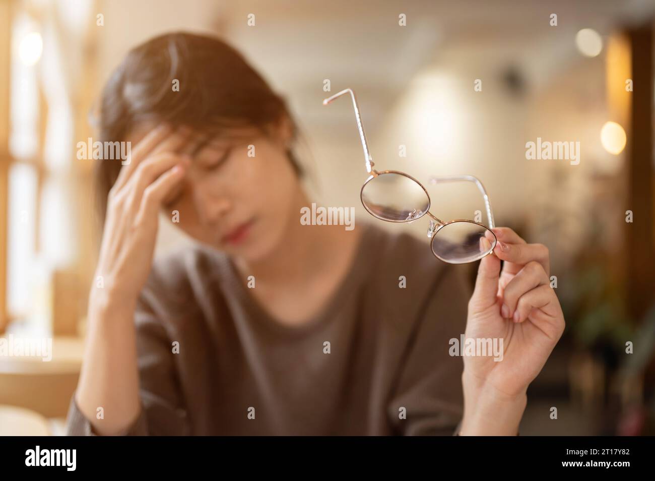 A stressed and tired young Asian woman is taking off her eyeglasses ...