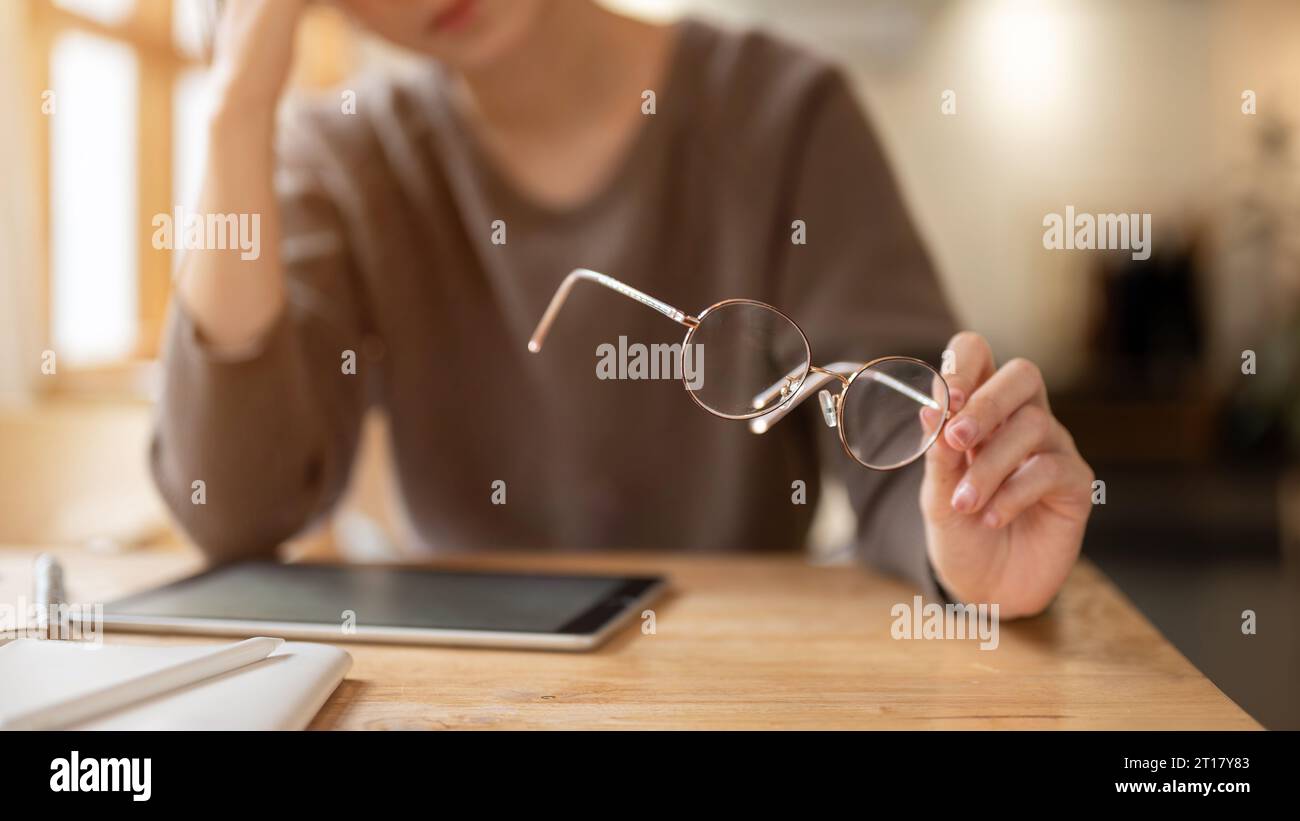 A stressed and tired woman is taking off her eyeglasses, suffering from ...