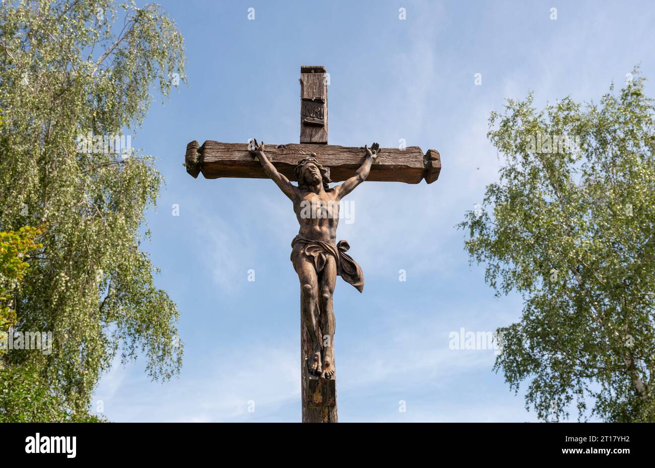 statue of jesus on cross between two trees against blue summer sky ...