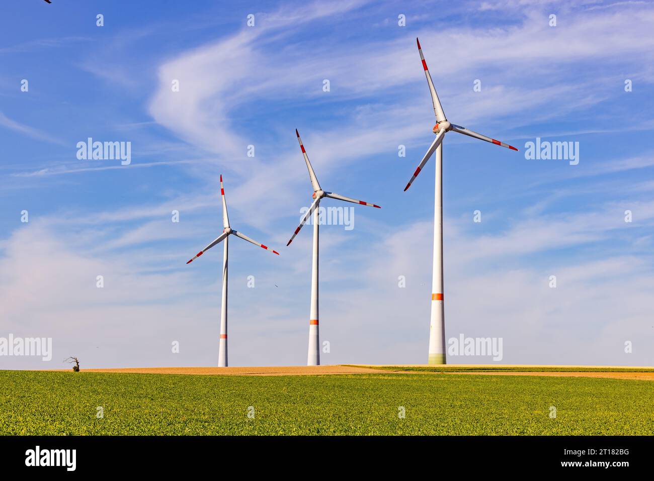 Three wind turbines of different sizes on an agricultural field next to ...