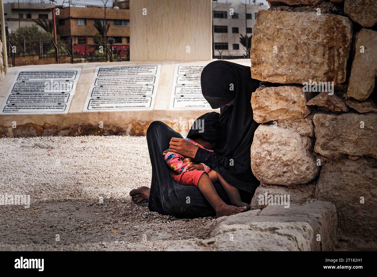 A poor Muslim woman in a black hijab sits on the ground and holds her ...