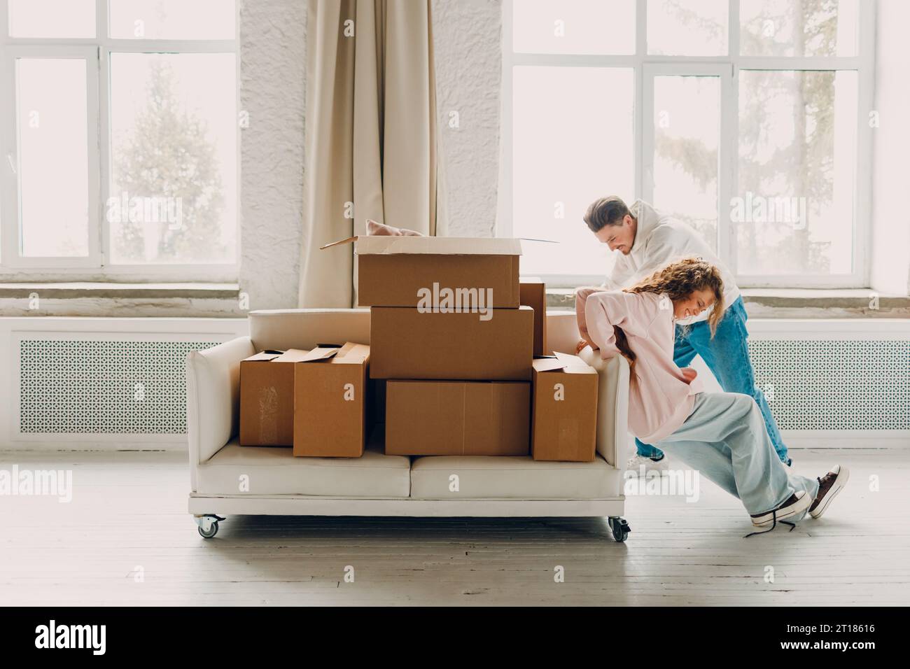 Happy young family couple man and woman push sofa with cardboard boxes ...