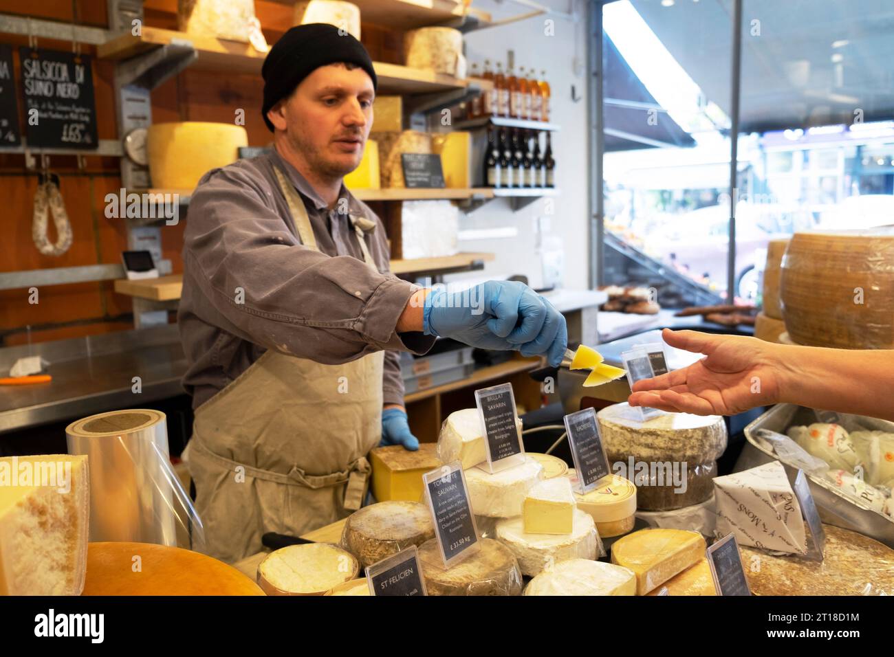 Interior view of Mons Cheesemongers shop worker giving customer a piece ...