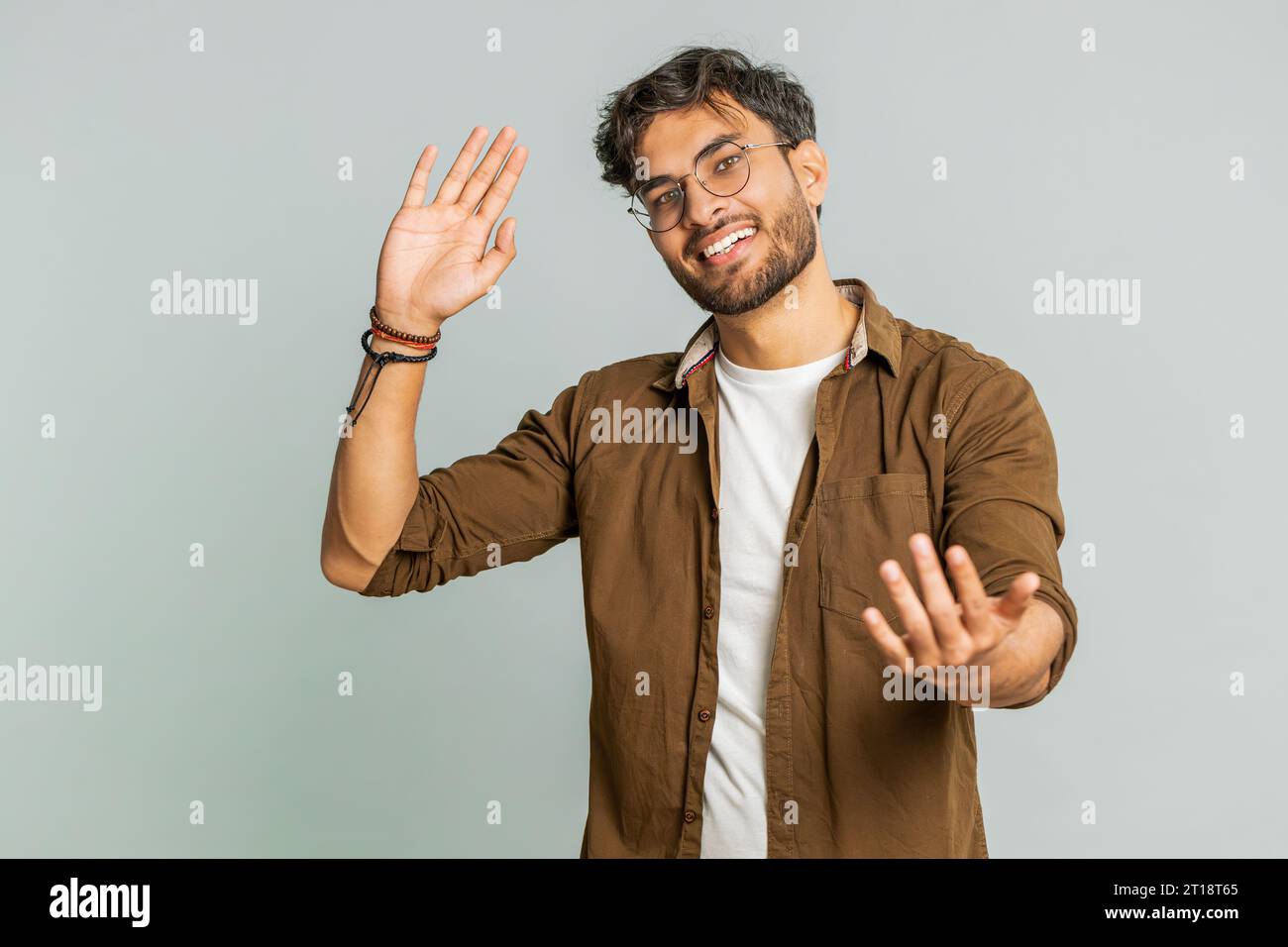 Young Indian man smiling friendly at camera, waving hands gesturing ...
