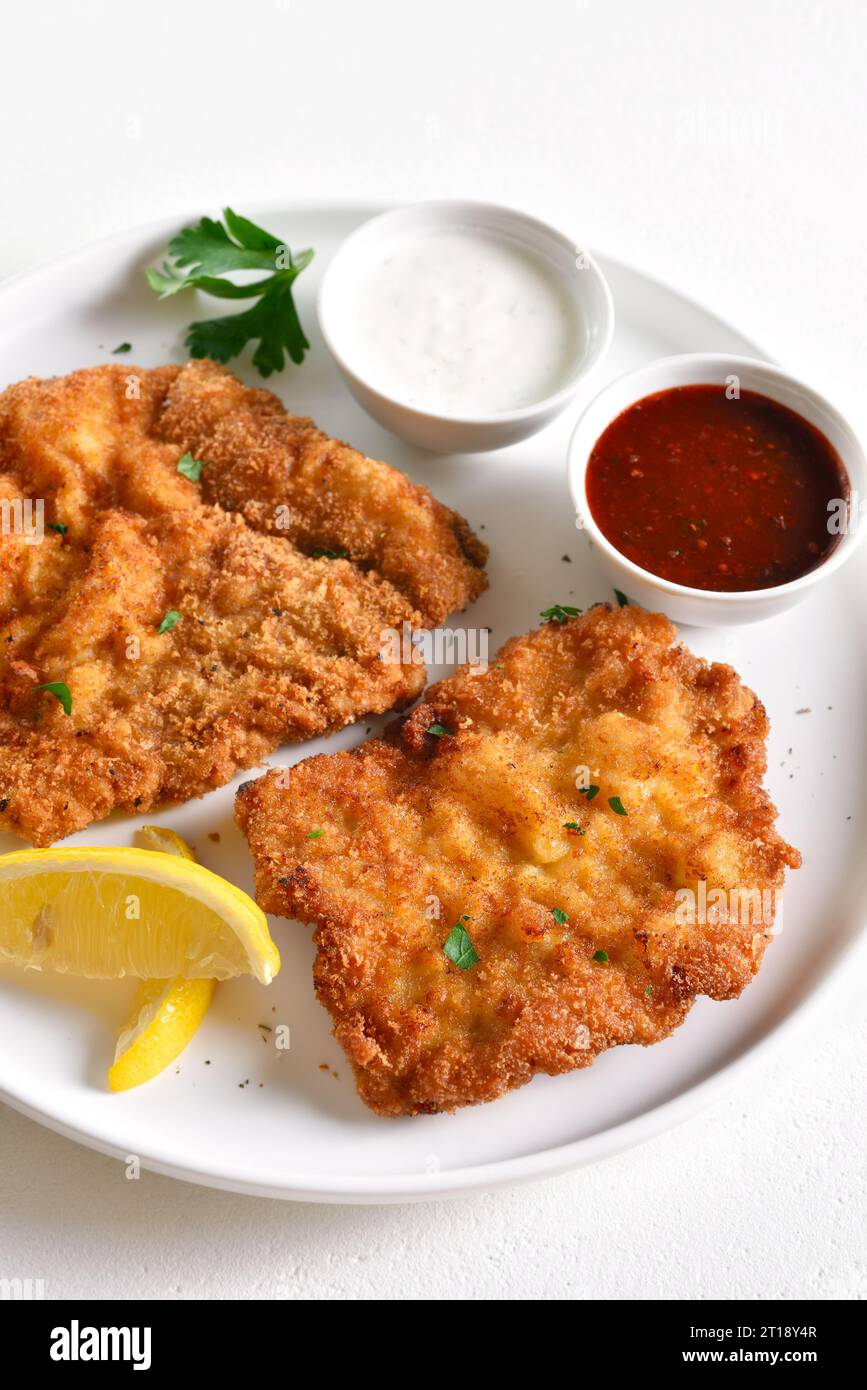 Breaded wiener schnitzel with sauce on plate over white background ...