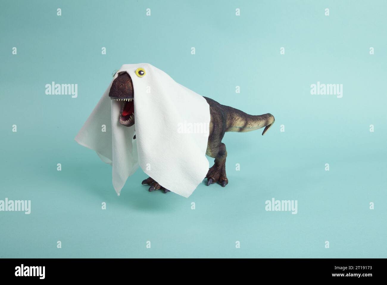 a plastic t-rex dinosaur figurine disguised as a ghost with a sheet and ...