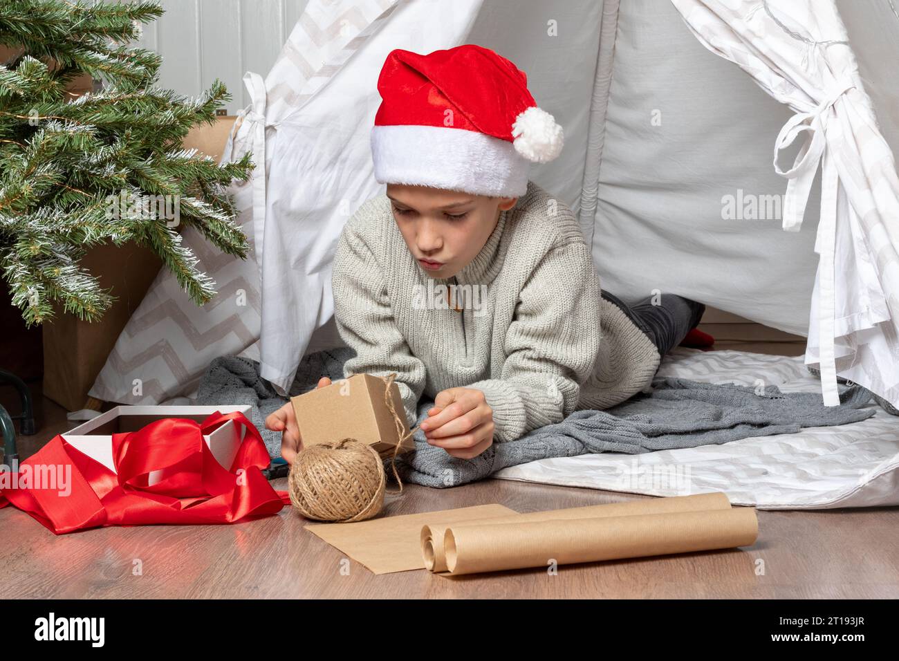 Gift wrapping. A child in a red Santa hat wraps Christmas gifts ...