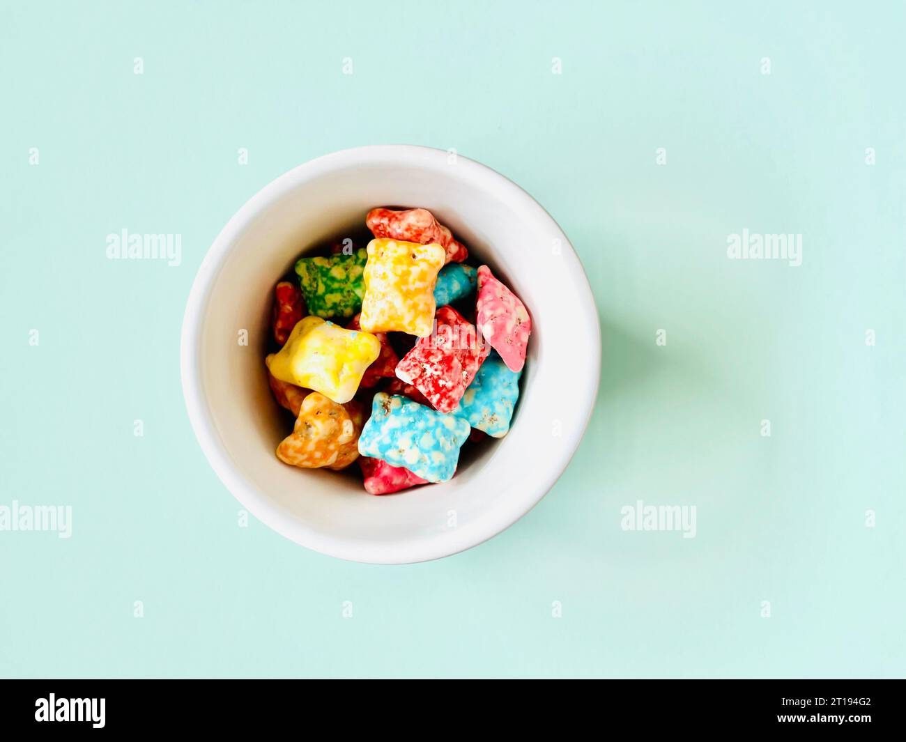 Overhead view of a bowl of multi coloured sweets on a turquoise ...