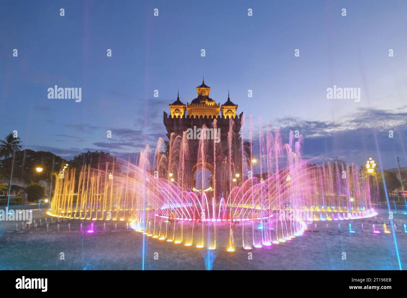 Illuminated water fountain in front of Patuxai (Patuxay) at dusk ...