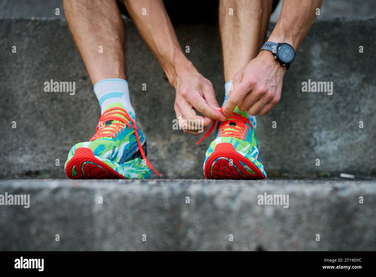 Athletic man tying his running shoes before exercising. Male runner at ...